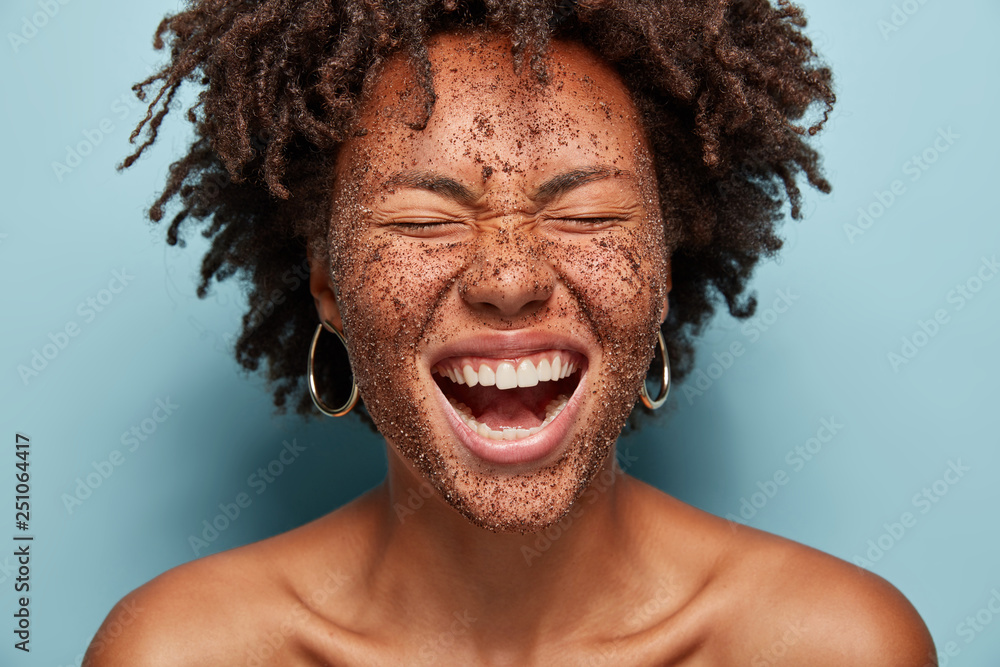 Overjoyed woman laughs loudly, cleans face skin with coffee scrub, has ...