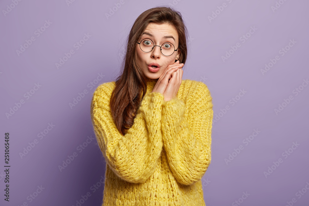 Dark haired young lady looks with wondered expression, keeps hands near ...
