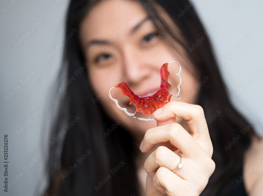 Portrait of beautiful Asian patient woman holding orthodontic retainers ...