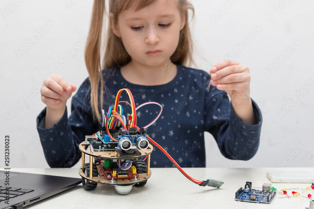 Cute little girl codes a metal car robot and an electronic board ...