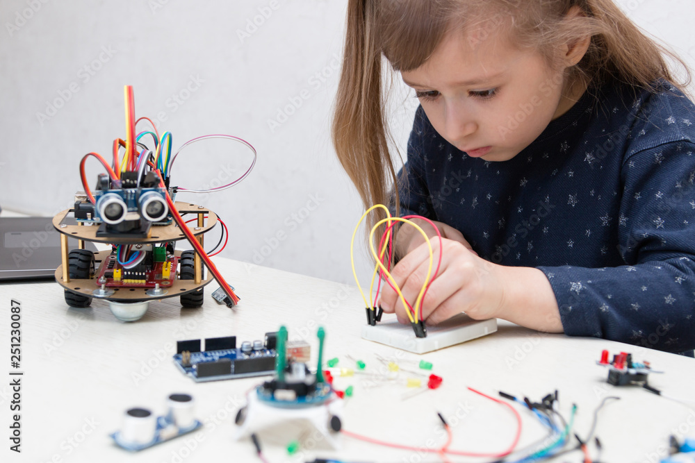 Cute little girl codes a metal car robot and an electronic board ...