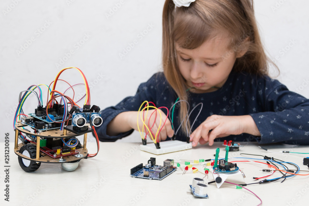 Cute little girl codes a metal car robot and an electronic board ...