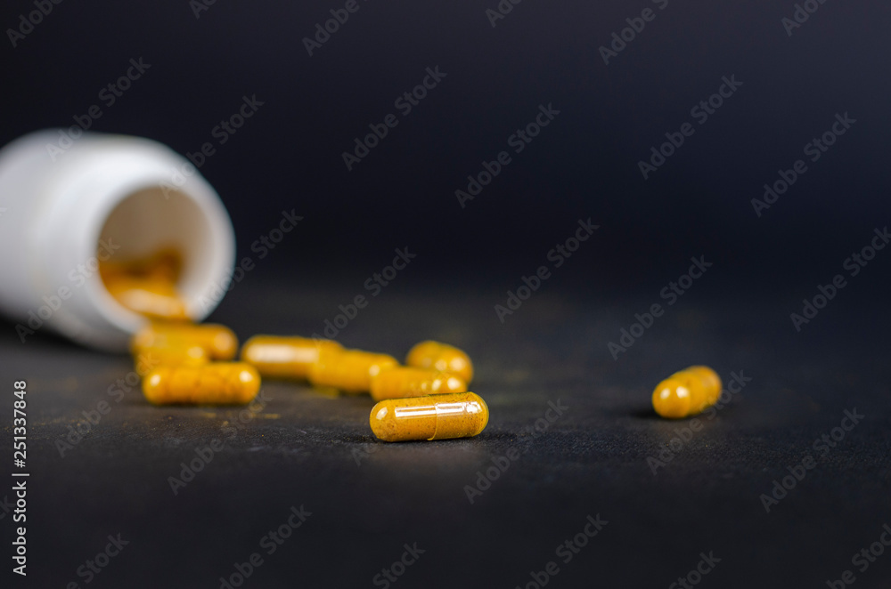 Yellow turmeric root powder capsules spilling out of a drug container ...