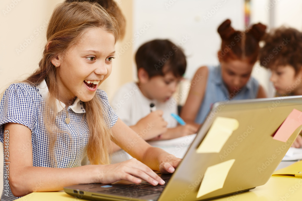 Curious pretty schoolgirl using laptop and typing in classroom. Smart ...