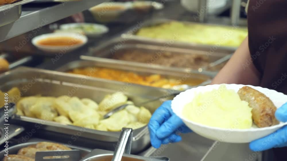 close-up, canteen worker lays a portion of mashed potatoes on the plate ...