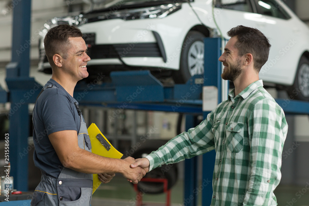Smiling worker of car service in uniform and satisfied client shaking ...
