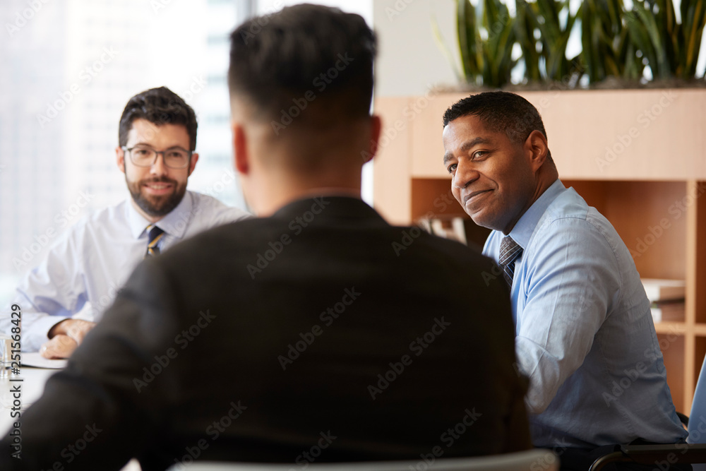 Three Businessmen Sitting Around Table Meeting In Modern Open Plan ...