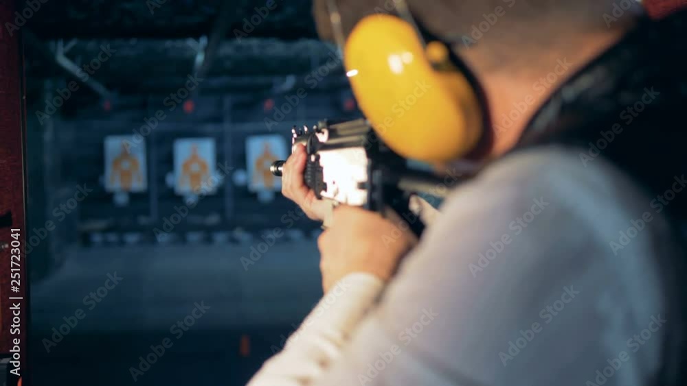 A man aiming a target with a rifle at a shooting range, back view ...