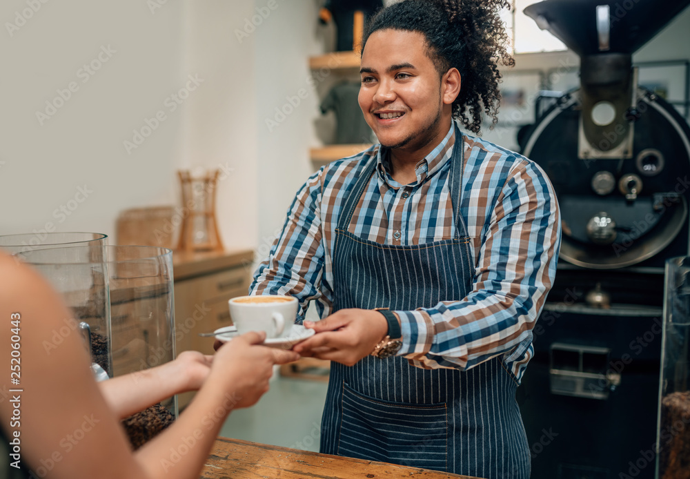 Young mixed raced barista handing over coffee to customer. With ...