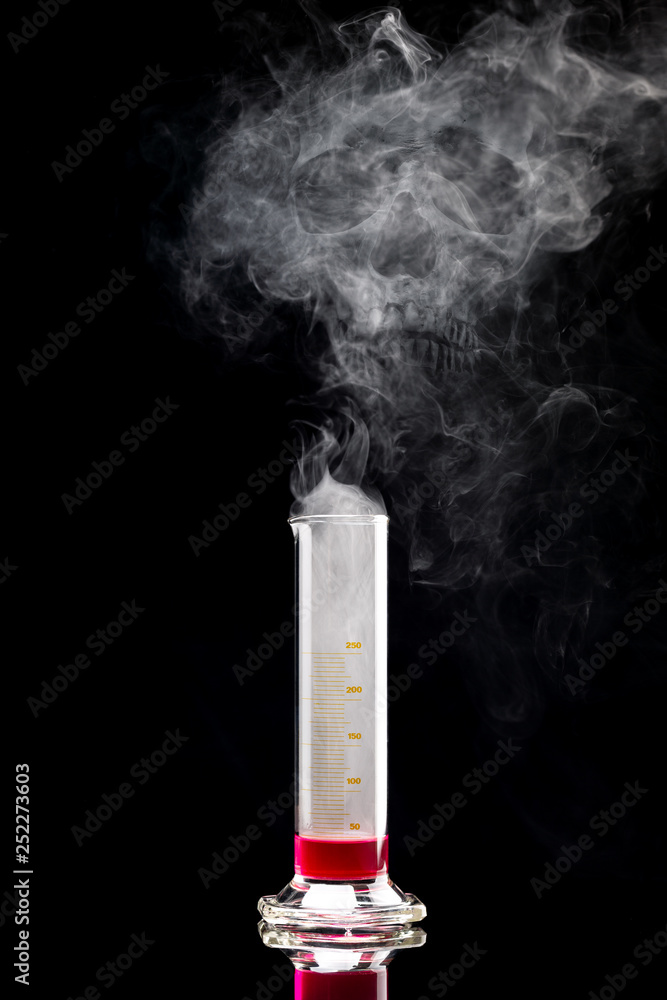 Graduated cylinder with red liquid on the tabel. Human skull appears in ...