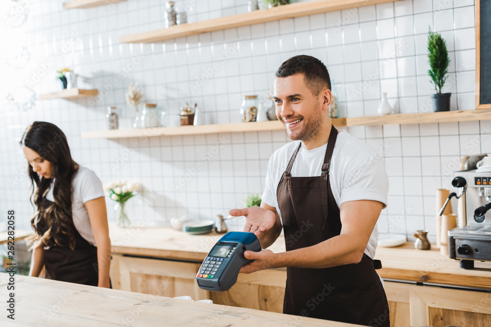 handsome cashier standing near bar counter and pointing to terminal ...