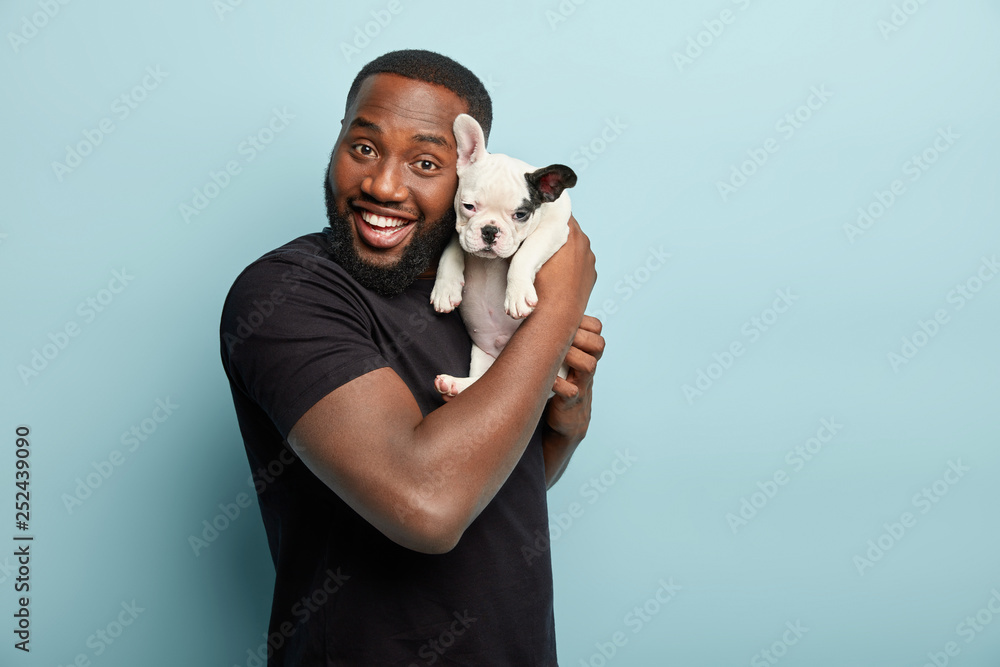 Happy satisfied smiling dark skinned man carries small pet of french ...