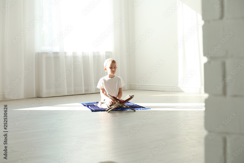 Little Muslim boy with Koran praying on rug indoors Stock Photo | Adobe ...