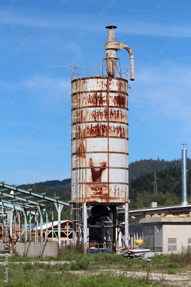 Tall partially rusted metal storage silo surrounded with destroyed ...