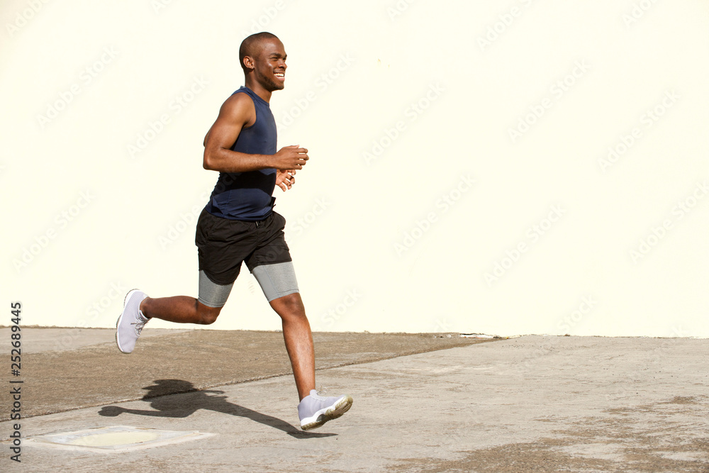 Full body happy young african american man running on street by wall ...