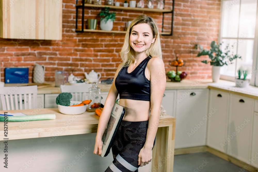 Close-up portrait of beautiful fit woman standing in her kitchen with a ...