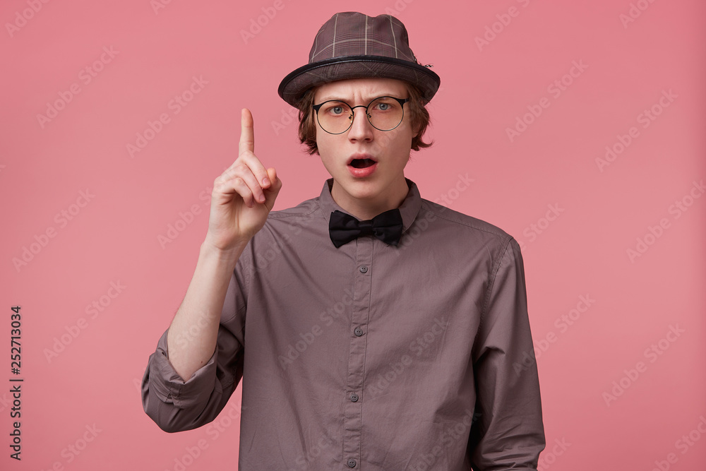 Serious young smartly dressed guy holding hand up pointing index finger ...