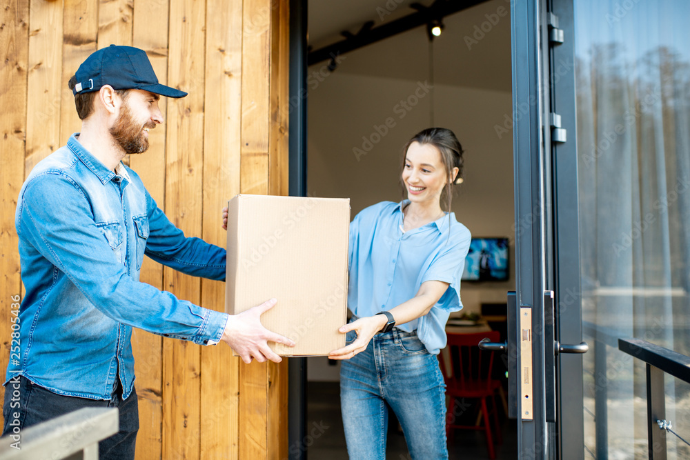 Delivery man bringing packaged goods to a young woman client standing ...