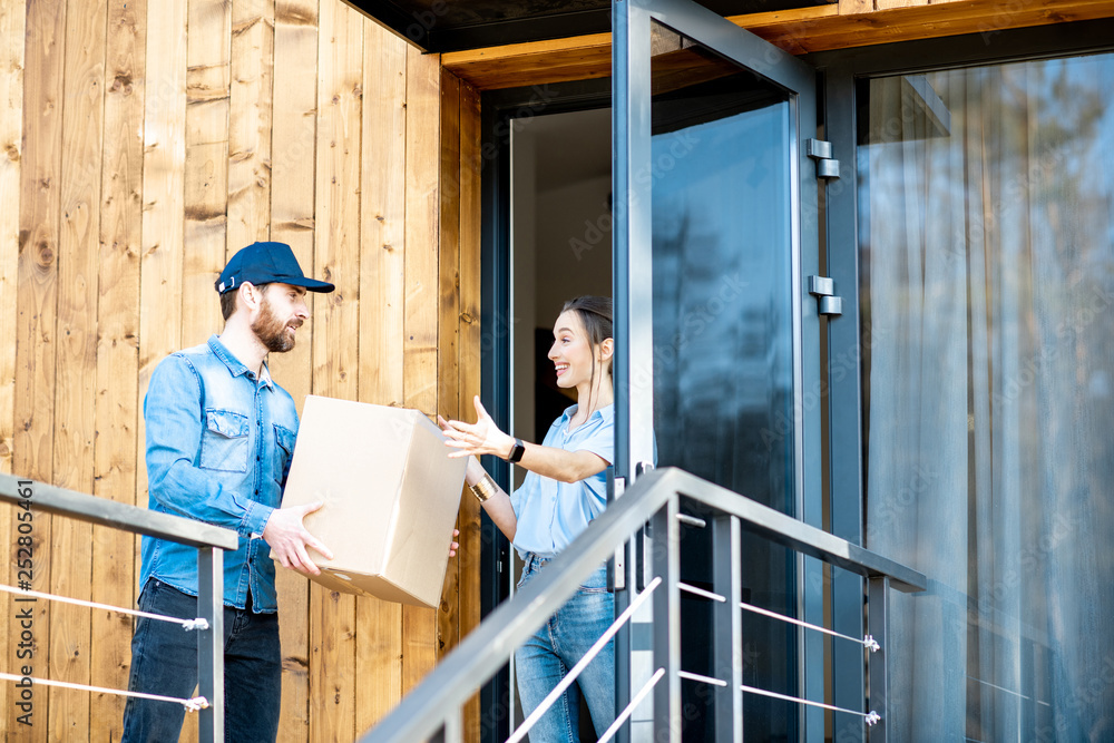 Delivery man bringing packaged goods to a young woman client standing ...