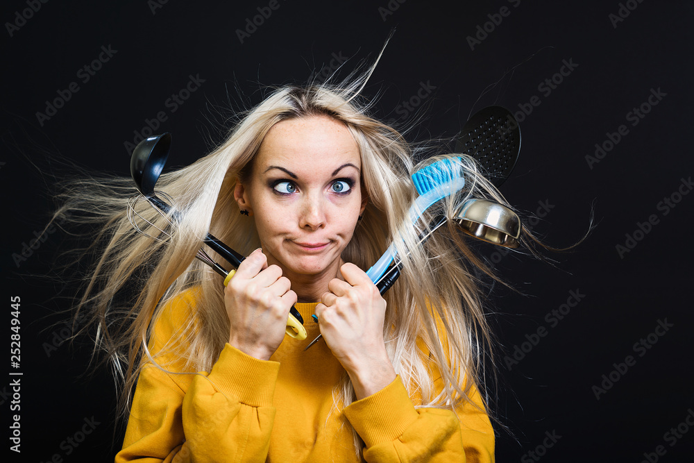 Crazy, disheveled girl with a ladle and kitchen utensils in her hands ...