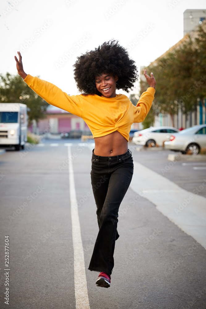 Young black woman with afro jumps, looking to camera, while crossing ...