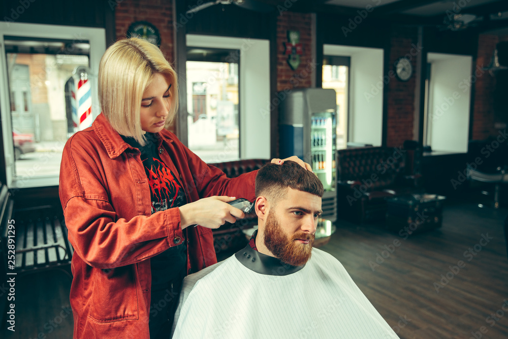 Client during beard shaving in barbershop. Female barber at salon ...