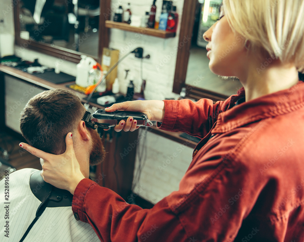 Client during beard shaving in barbershop. Female barber at salon ...