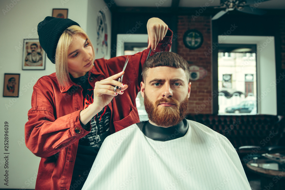 Client during beard shaving in barbershop. Female barber at salon ...