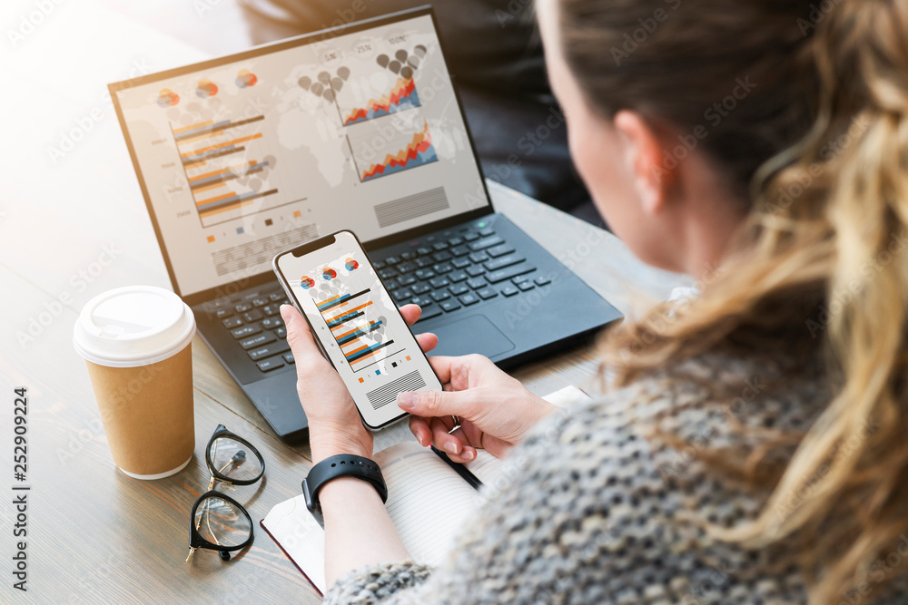 Laptop with graphs, charts, diagrams on screen.Girl tusing smartphone ...