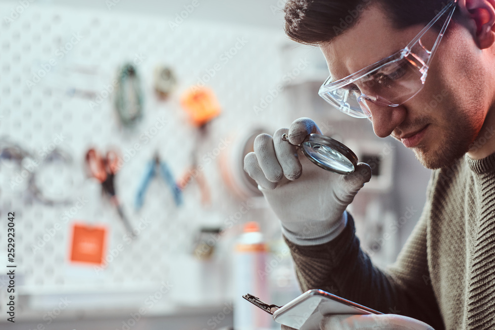 The technician uses a magnifying glass to carefully inspect the ...