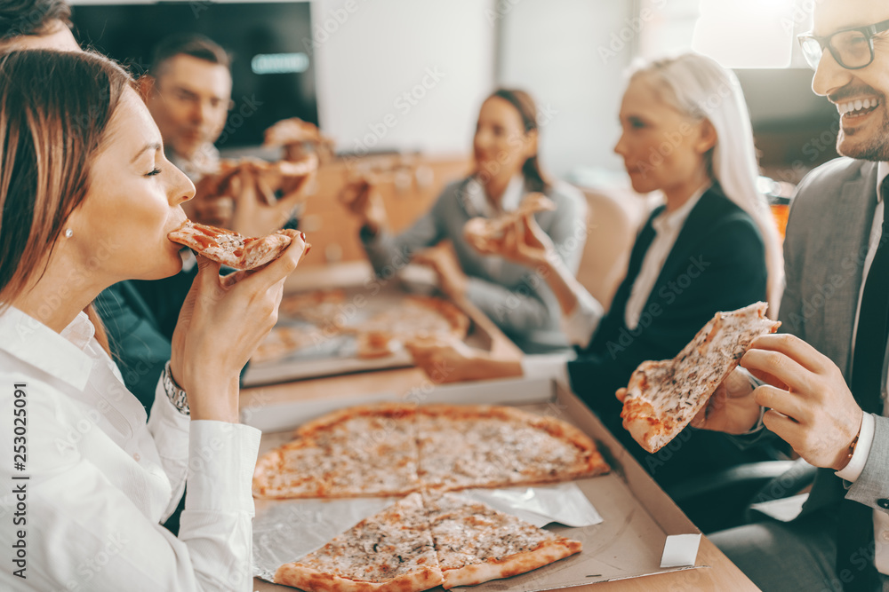 Small group of happy colleagues in formal wear eating pizza together ...