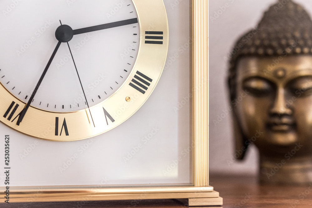 golden and white clock in front of a white wall and a buddha statue ...