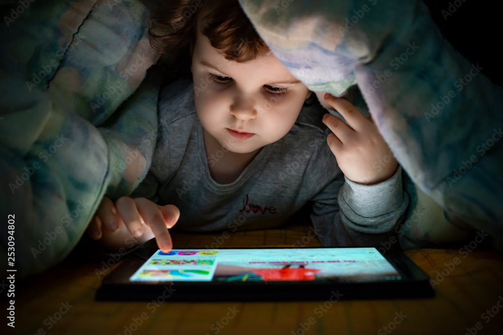 Little girl watching her tablet in the bed. Illuminated child face from ...