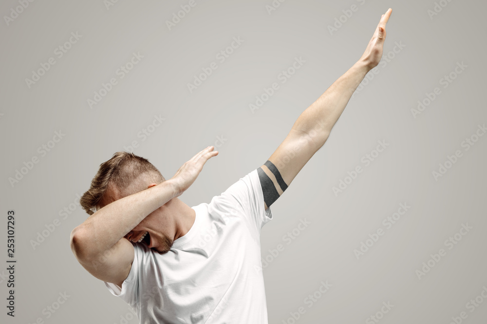 Young man makes a dab movement with his arms on a gray background ...