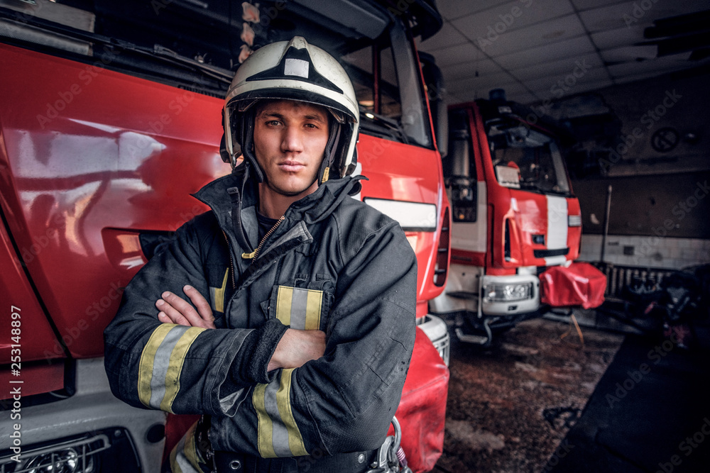 Confident fireman wearing protective uniform standing next to a fire ...