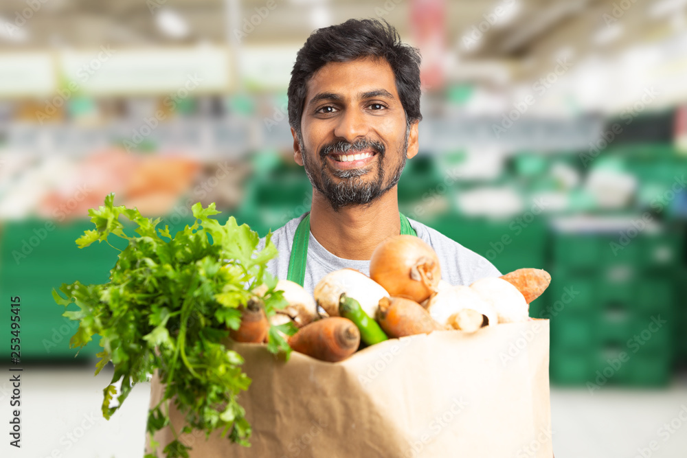 Grocery store employee holding bag of vegetables. Stock Photo | Adobe Stock