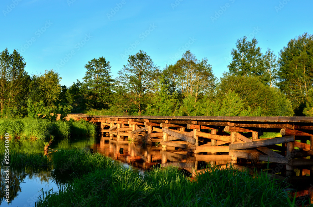 A wooden bridge of tree logs lies across a small river inside a wooded ...