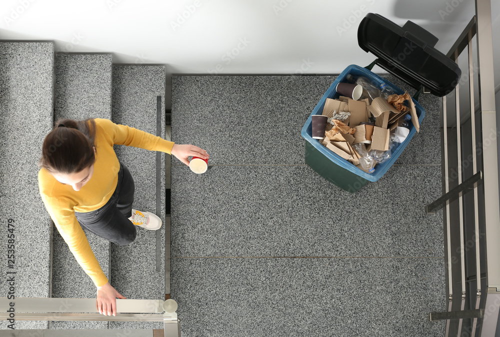 Young woman throwing coffee cup in trash bin indoors, top view. Waste ...