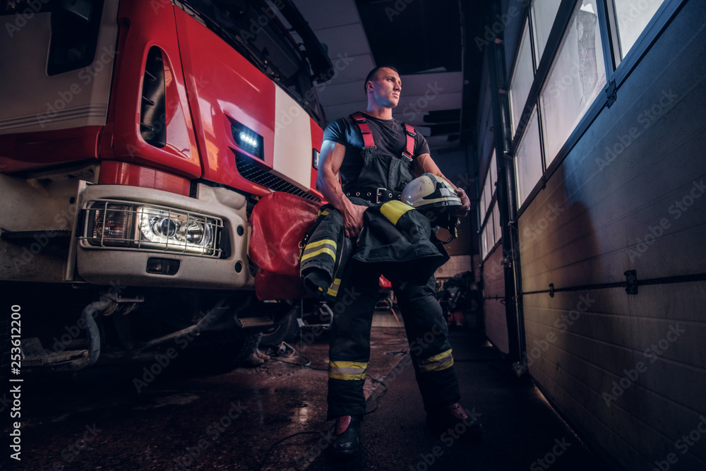 Muscular fireman holding a protective helmet in a garage of a fire ...