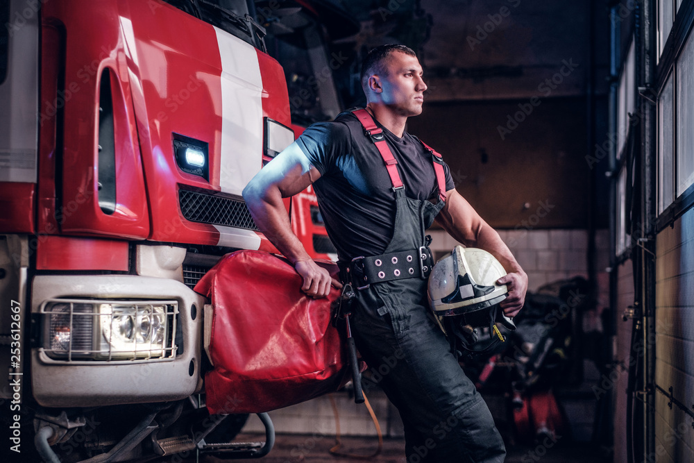 Muscular fireman holding a protective helmet in a garage of a fire ...