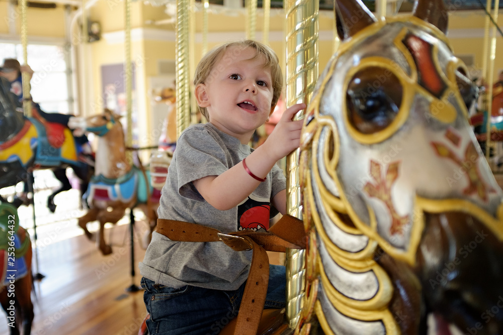 Young blond ,toddler aged ,blond haired boy ,riding a brown carousel ...