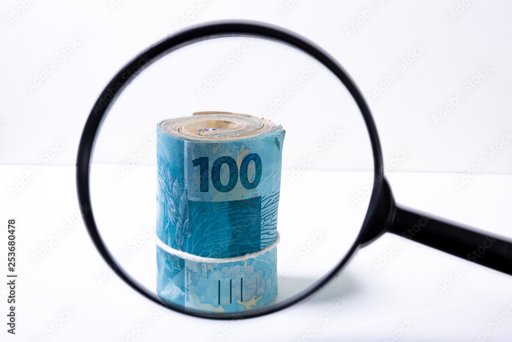 Focus on a thick roll of banknotes seen through a magnifying glass lit ...