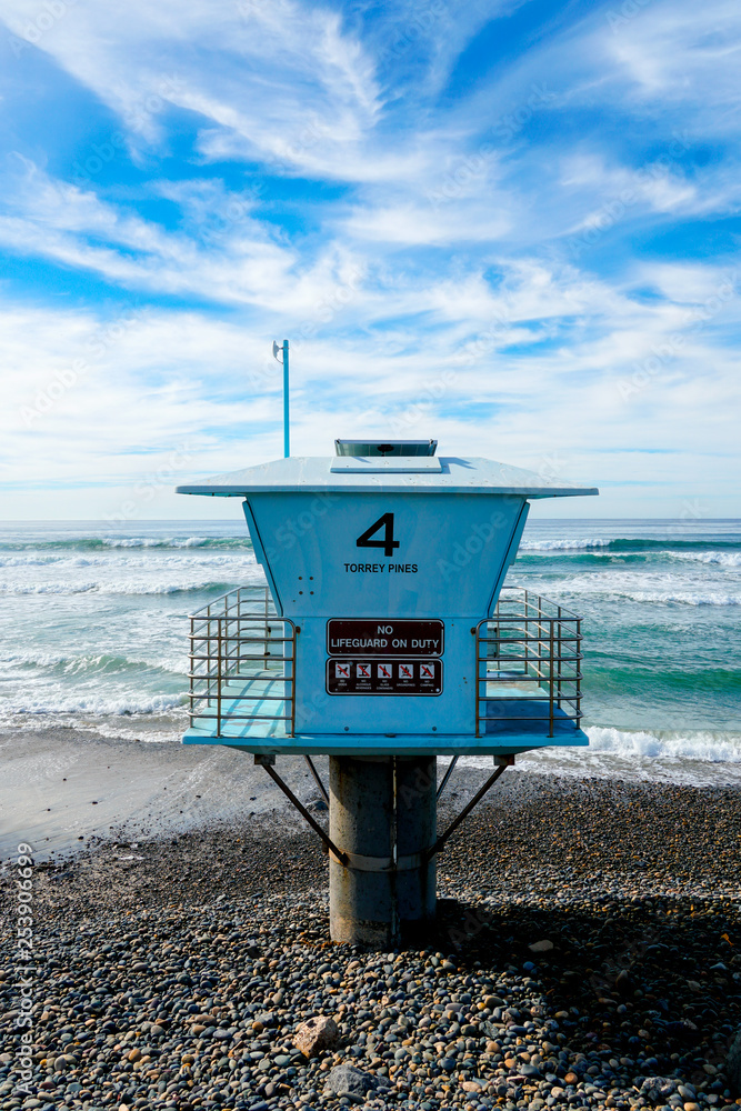 Blue lifeguard tower on a rocky sand beach with clouded blue sky sunny ...