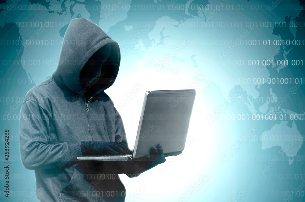 Hacker in black hoodie holding laptop with binary code on virtual ...