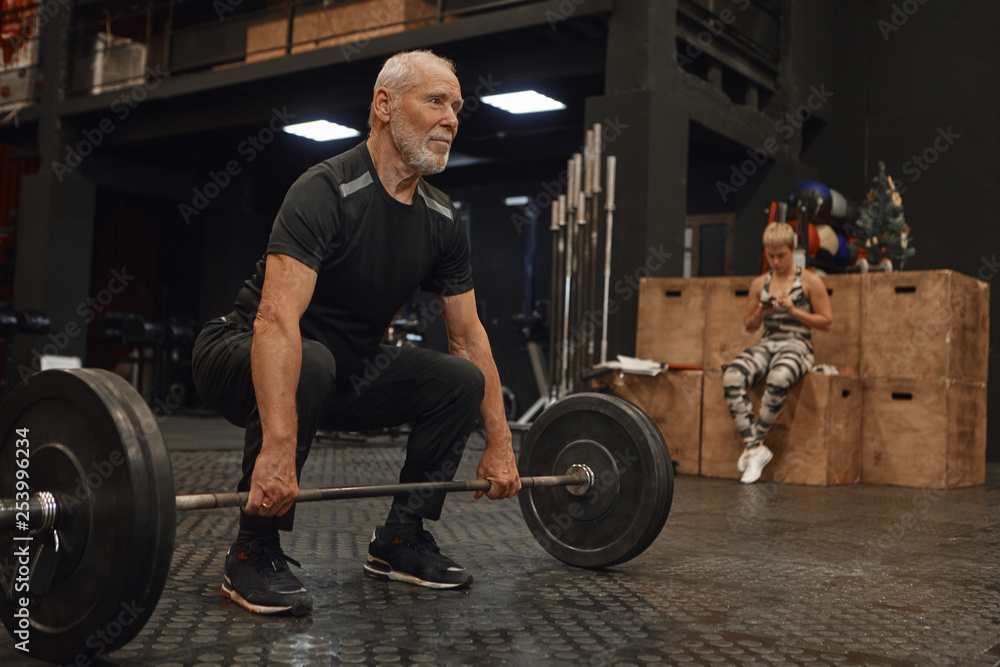 Elderly mature male with thick gray beard lifting barbell with weight ...