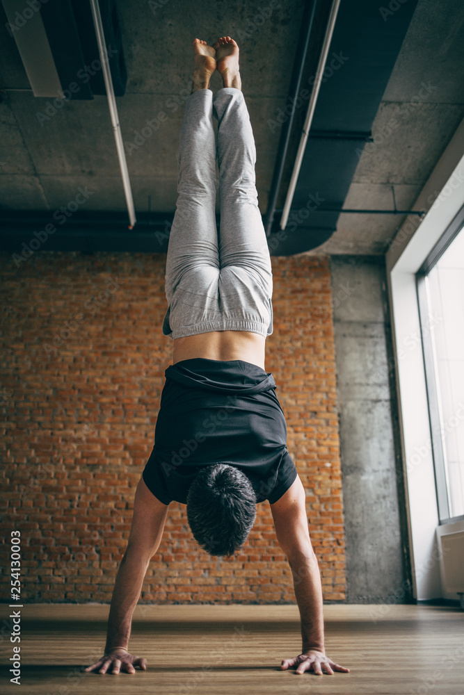 Young man doing yoga handstand in big bright training gym Stock Photo ...