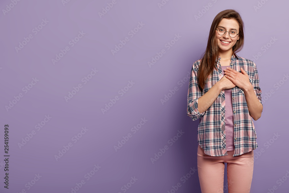Positive delighted woman feels thankful, keeps both hands on chest ...