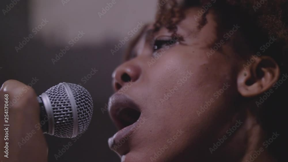 Close up side view of one young African female singer singing and ...