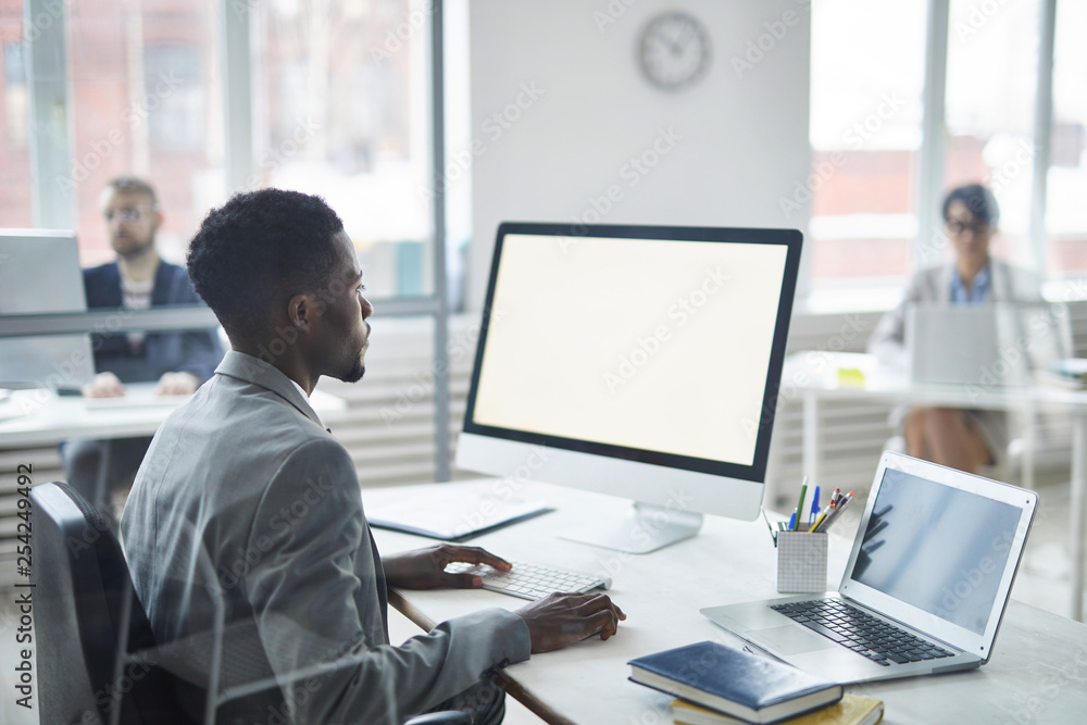 Young confident broker looking at computer screen while searching for ...