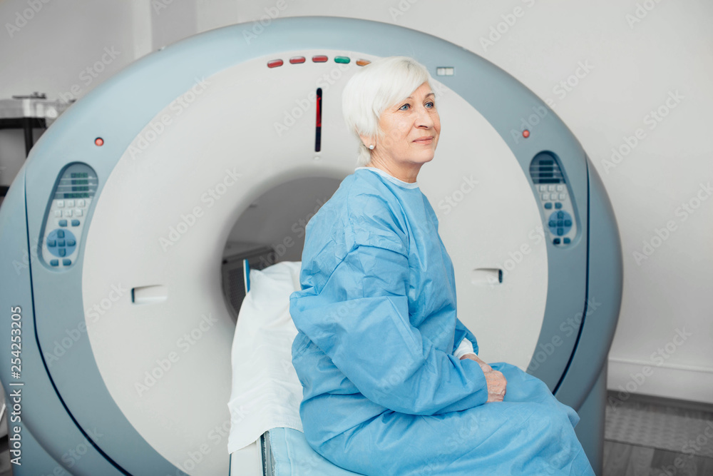 Pensive elderly woman sitting on scanner table. waiting for CT scan ...